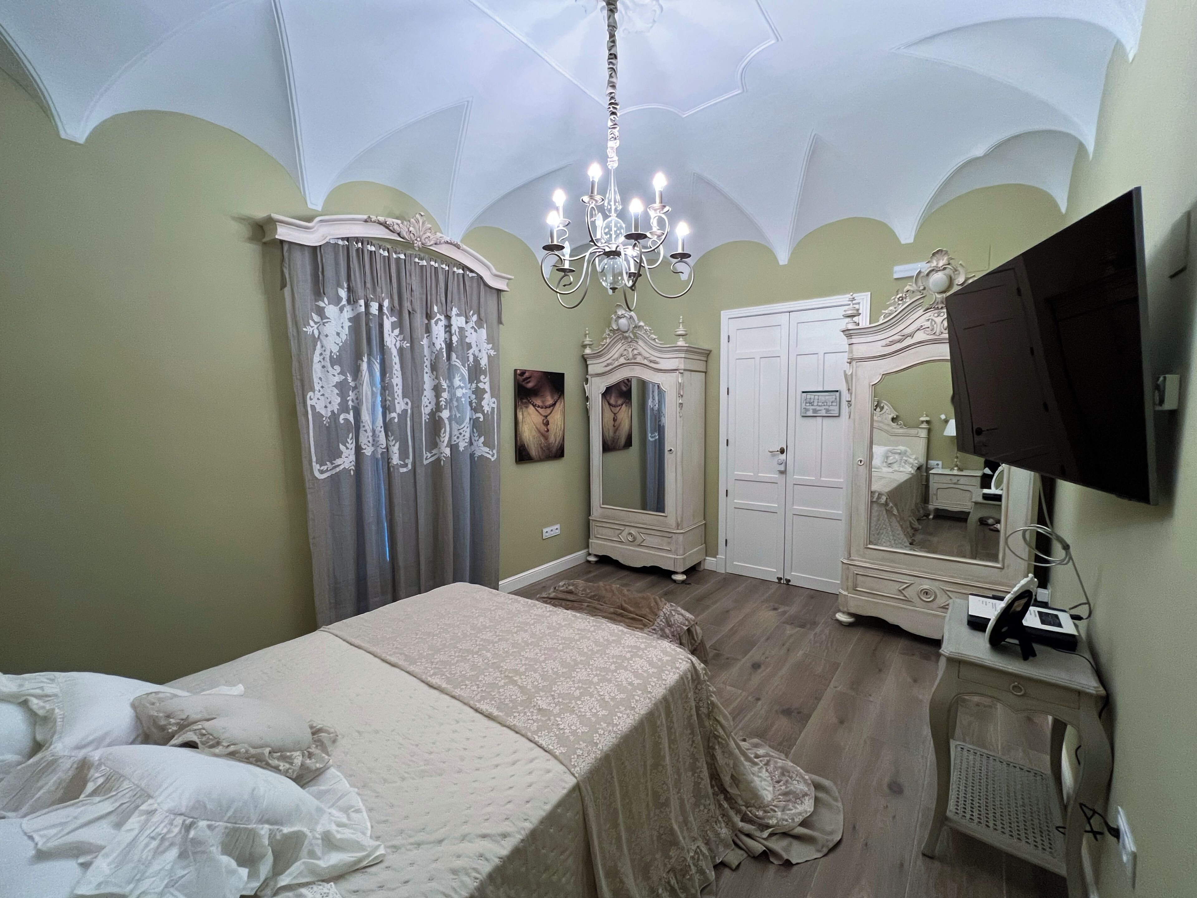 Quarto com cama, lustre, guarda-roupa, espelho e televisão.
