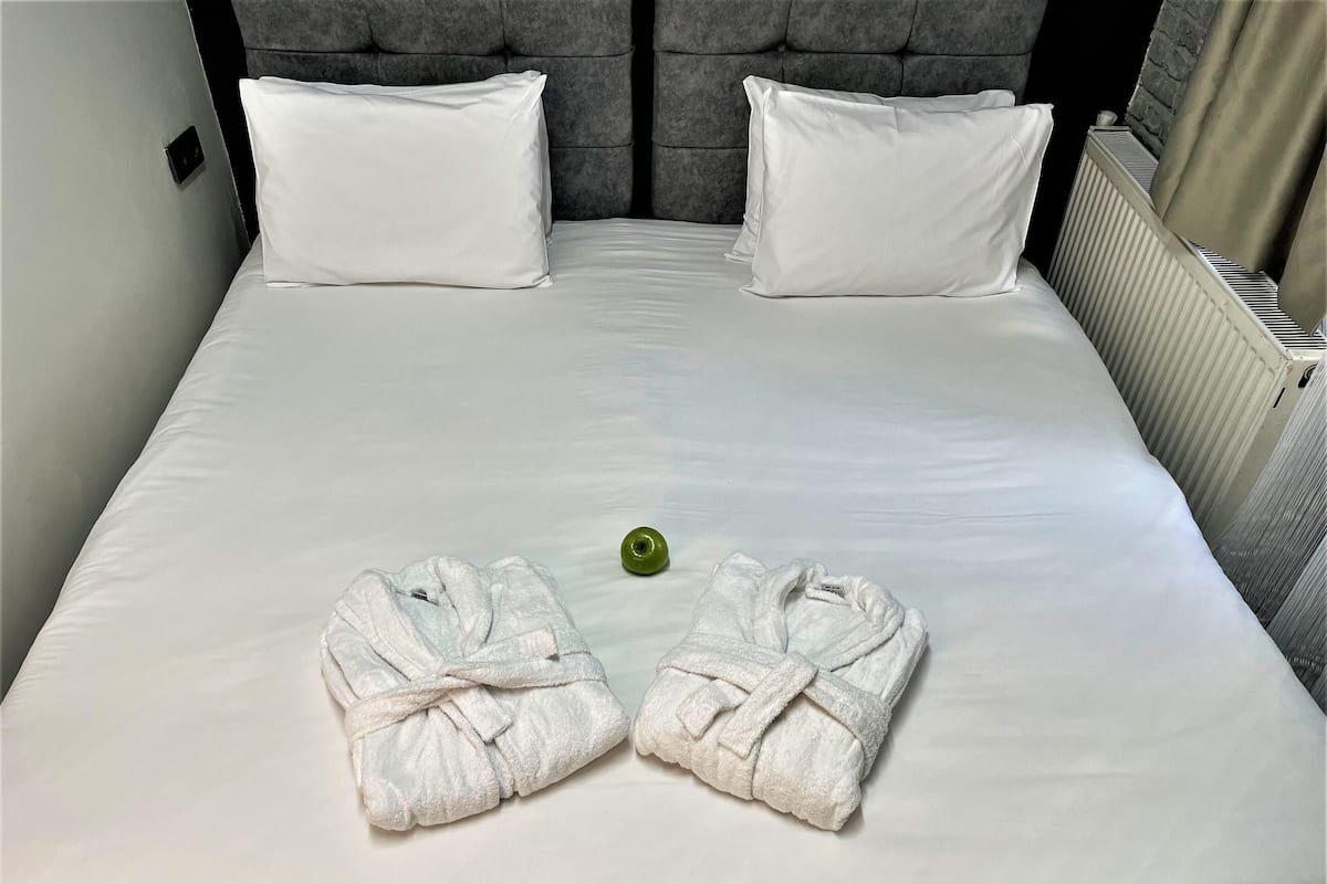 Cama bem arrumada com duas almofadas, um par de toalhas e uma maçã verde sobre a cama.