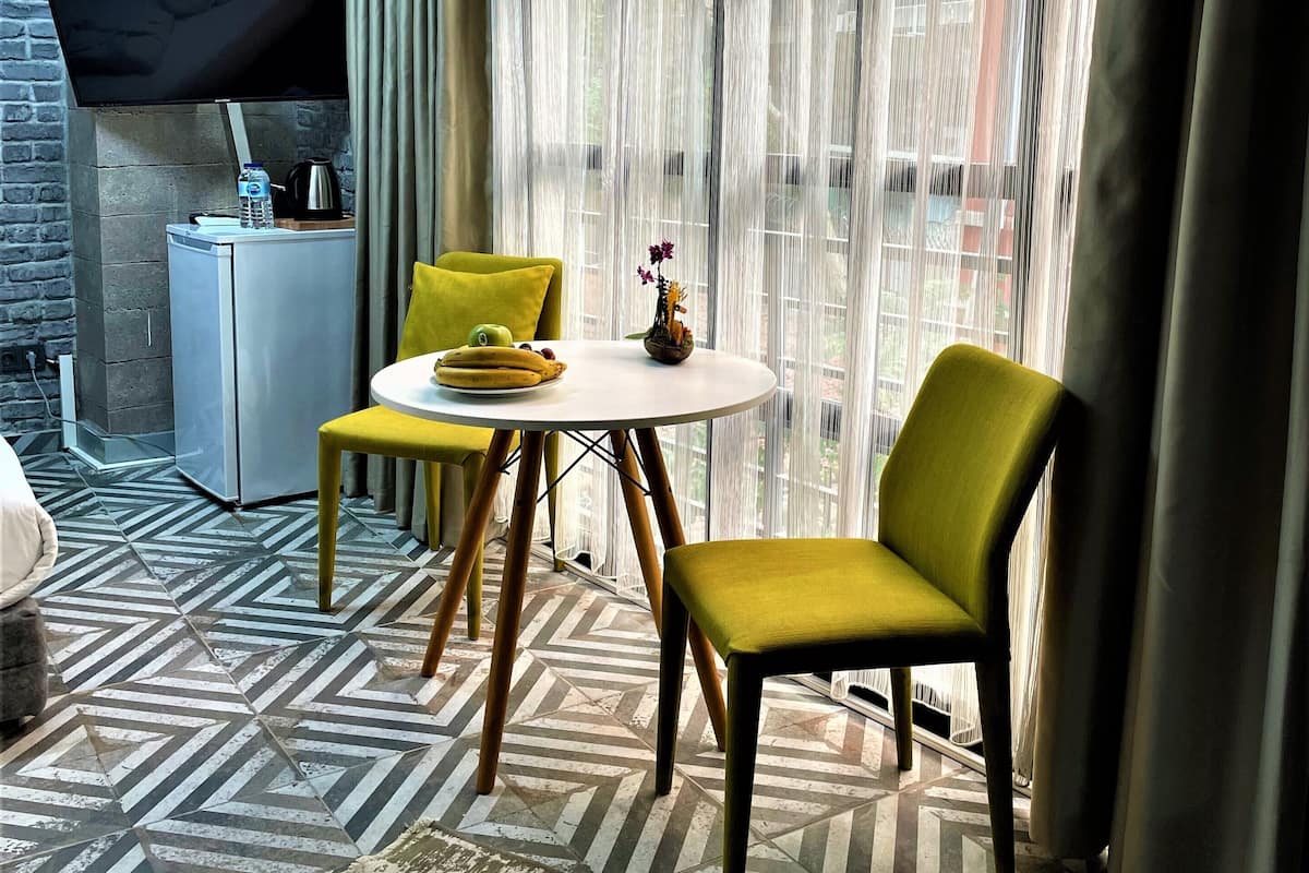 Quarto moderno com mesa de jantar, duas cadeiras, TV de tela plana, mini-geladeira e uma planta decorativa.
