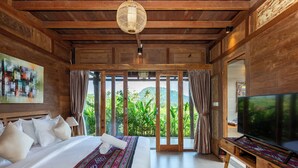 Quarto espaçoso com cama grande, televisão e vista para vegetação exuberante.