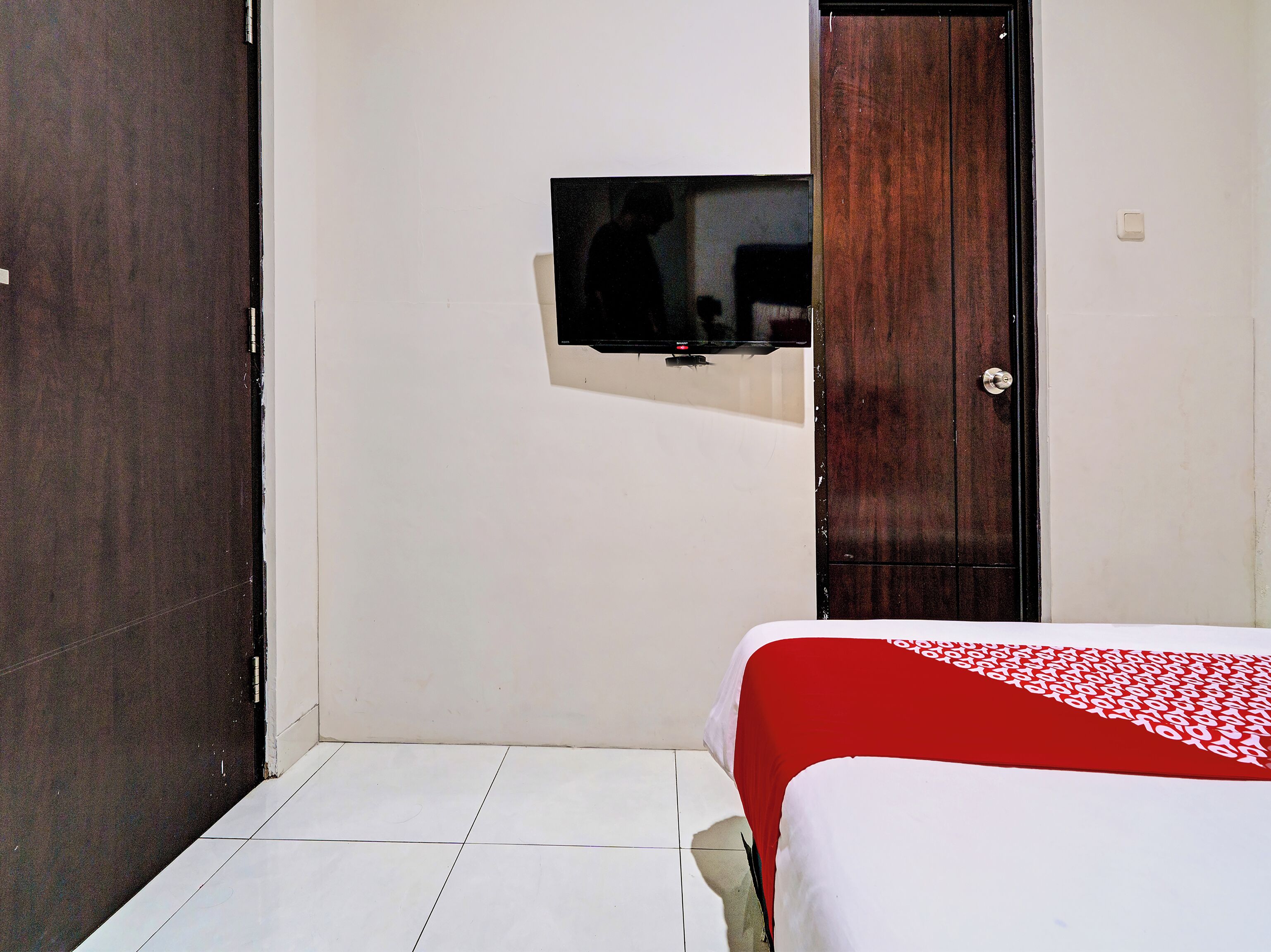 Quarto de hotel com uma cama, televisão fixada na parede e porta de madeira.