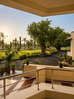 Uma varanda de hotel com vista para um jardim bem cuidado, incluindo uma grande árvore e palmeiras.