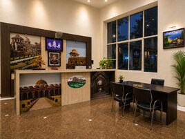 Um balcão de recepção com uma tela digital, fotografias emolduradas e uma placa para o Hotel TGI Jahaj Mahal.