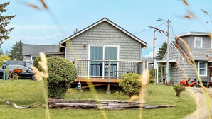 Uma casa residencial com gramado frontal, cerca de madeira e entrada com calçamento de brita.