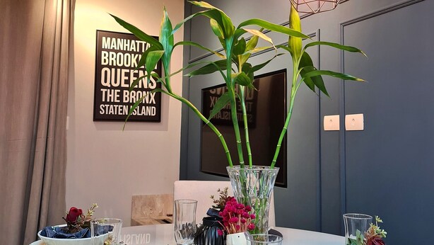 Mesa de jantar posta com pratos, talheres e objetos decorativos, incluindo um vaso com plantas e flores.
