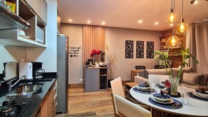 Cozinha moderna com fogão embutido, área de jantar com mesa redonda e sala de estar com sofá.