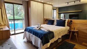 Quarto moderno com uma cama grande, uma escrivaninha e vista para o verde lá fora.