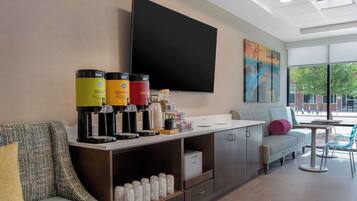 Um hall de hotel moderno com um sofá, um espaço de café e uma televisão de tela plana na parede.