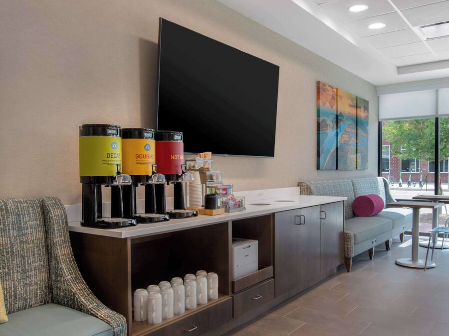 Um hall de hotel moderno com um sofá, um espaço de café e uma televisão de tela plana na parede.