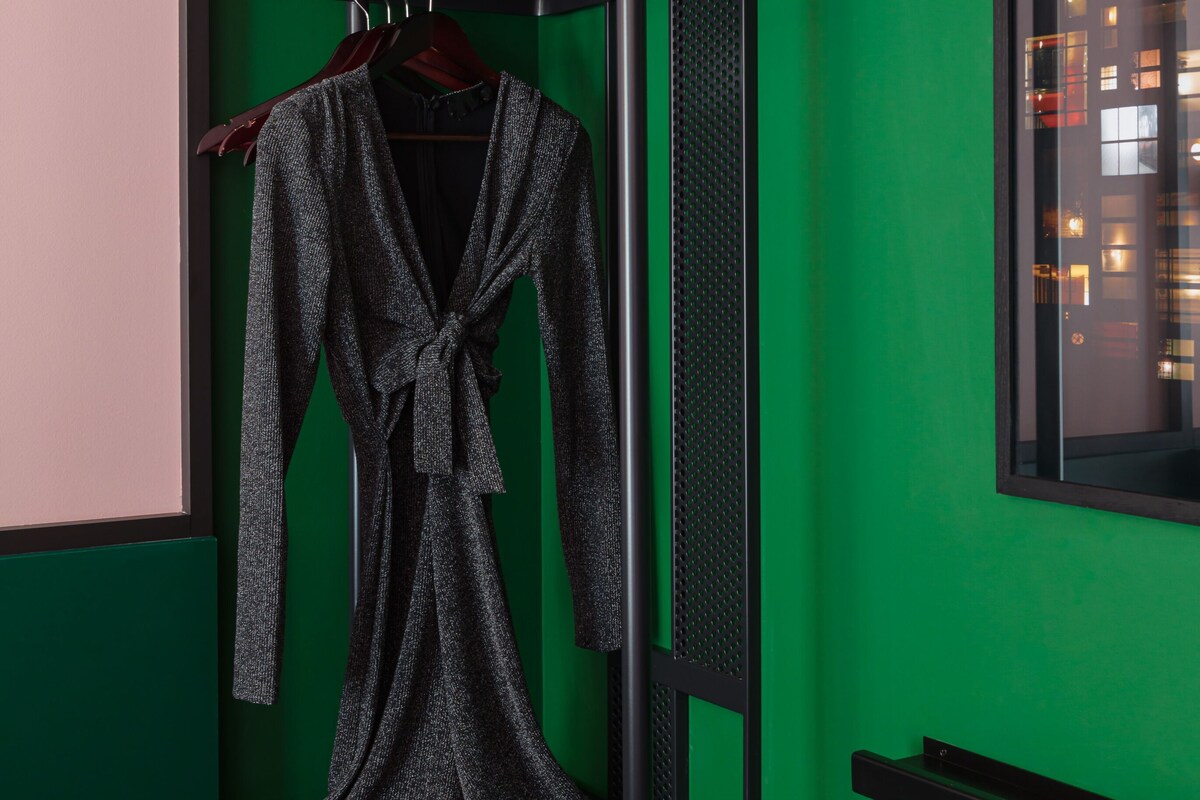 Quarto com parede verde, um suporte de metal preto e uma janela refletindo um horizonte urbano.