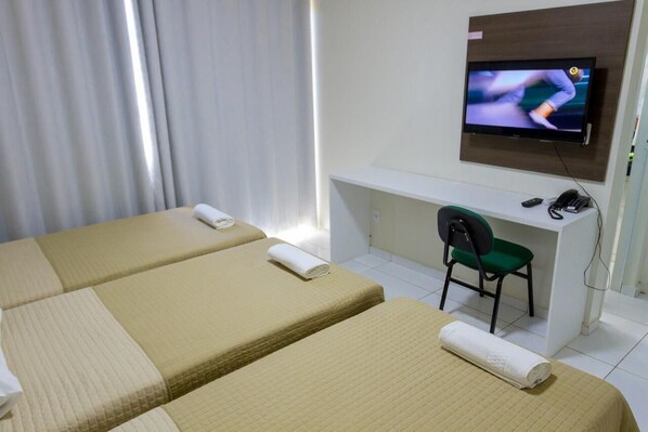 Quarto de hotel com duas camas, uma escrivaninha com cadeira, uma televisão e um telefone.