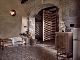 Um interior rústico com paredes de pedra, um banco de madeira, uma cesta de palha e um armário.
