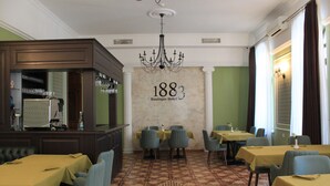 Uma sala de jantar com várias mesas e cadeiras, um lustre e uma parede com o número 1883.