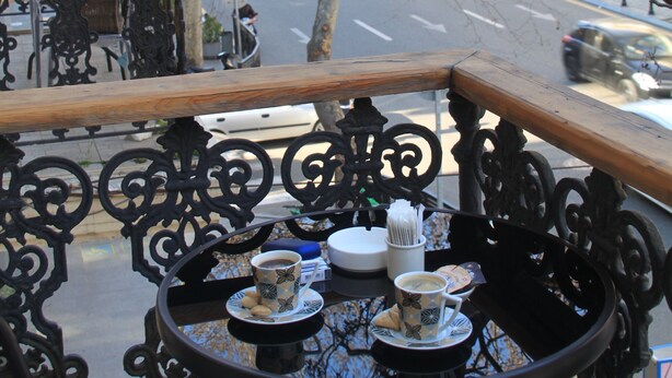 Varanda com mesa posta para dois, com vista para uma rua com carros e edifícios.
