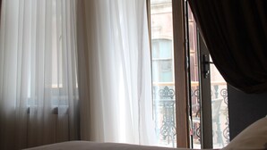 Quarto de hotel com cama, cortinas finas e vista para a varanda.