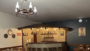 Interior de restaurante com área de bar, mesas e cadeiras de madeira e um candelabro.