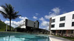 Piscina com água cristalina, rodeada por um espaço pavimentado e um edifício com design moderno.
