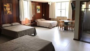 Quarto de hotel com duas camas de solteiro, uma mesa de jantar com cadeiras e uma cozinha compacta.