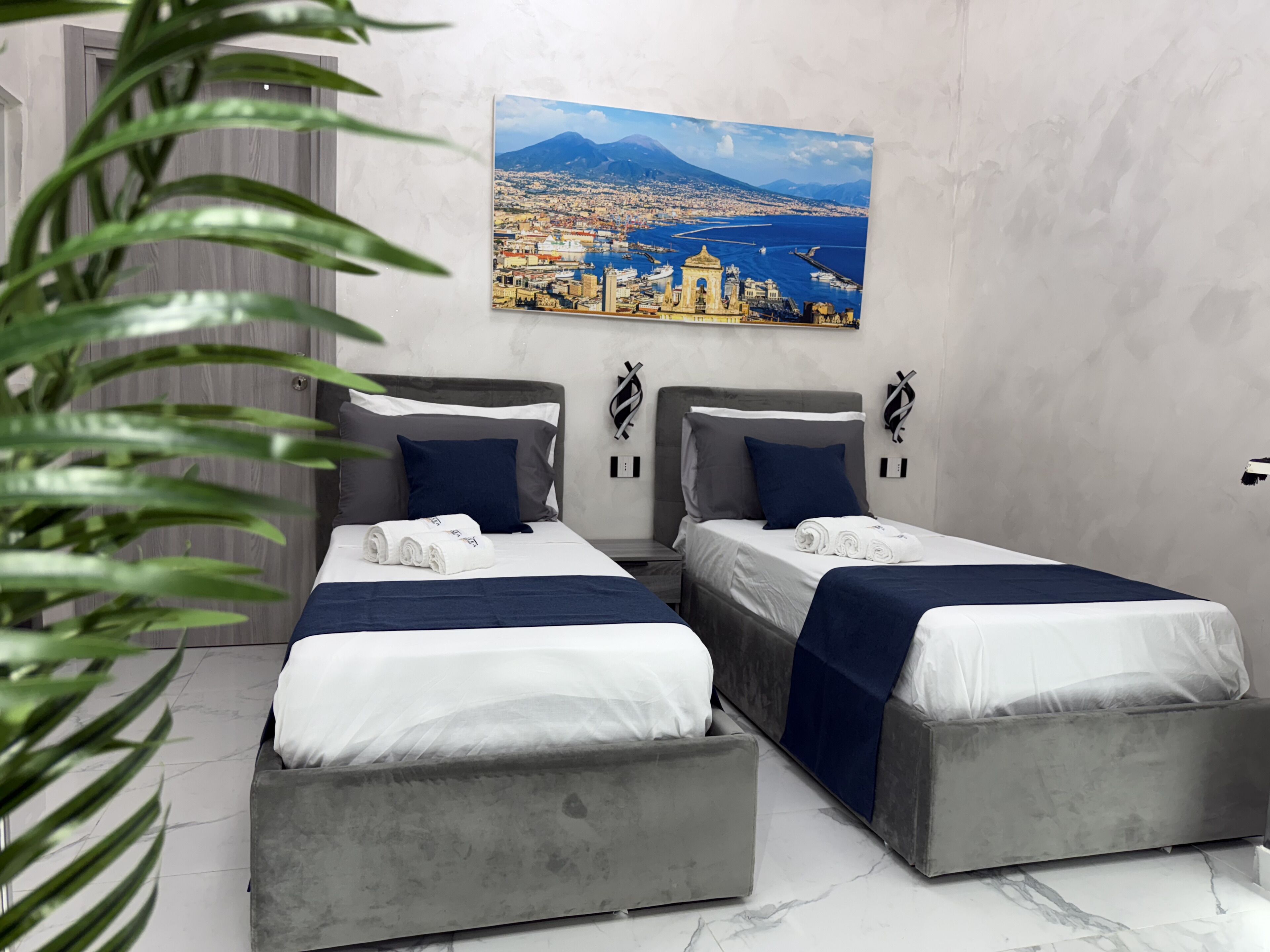 Quarto de hotel com duas camas, um quadro de paisagem urbana na parede e uma planta em primeiro plano.