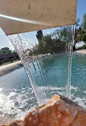Vista nítida de uma piscina com água escorrendo de uma torneira, refletindo árvores e um deck de madeira ao fundo.