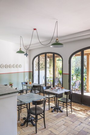Uma área de refeições com mesas e cadeiras, um balcão de cozinha e vista através de grandes janelas.