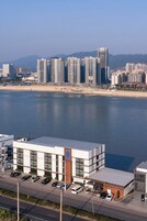 Um edifício moderno com estacionamento e vista para um corpo de água tranquilo, com edifícios altos ao fundo.