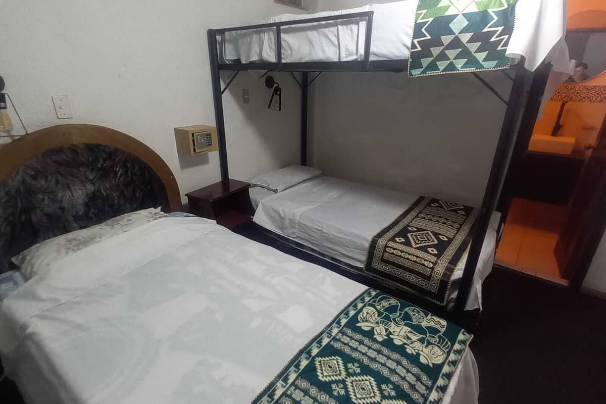 Quarto com beliche, cabeceira de madeira, mesa de cabeceira e coberta estampada.