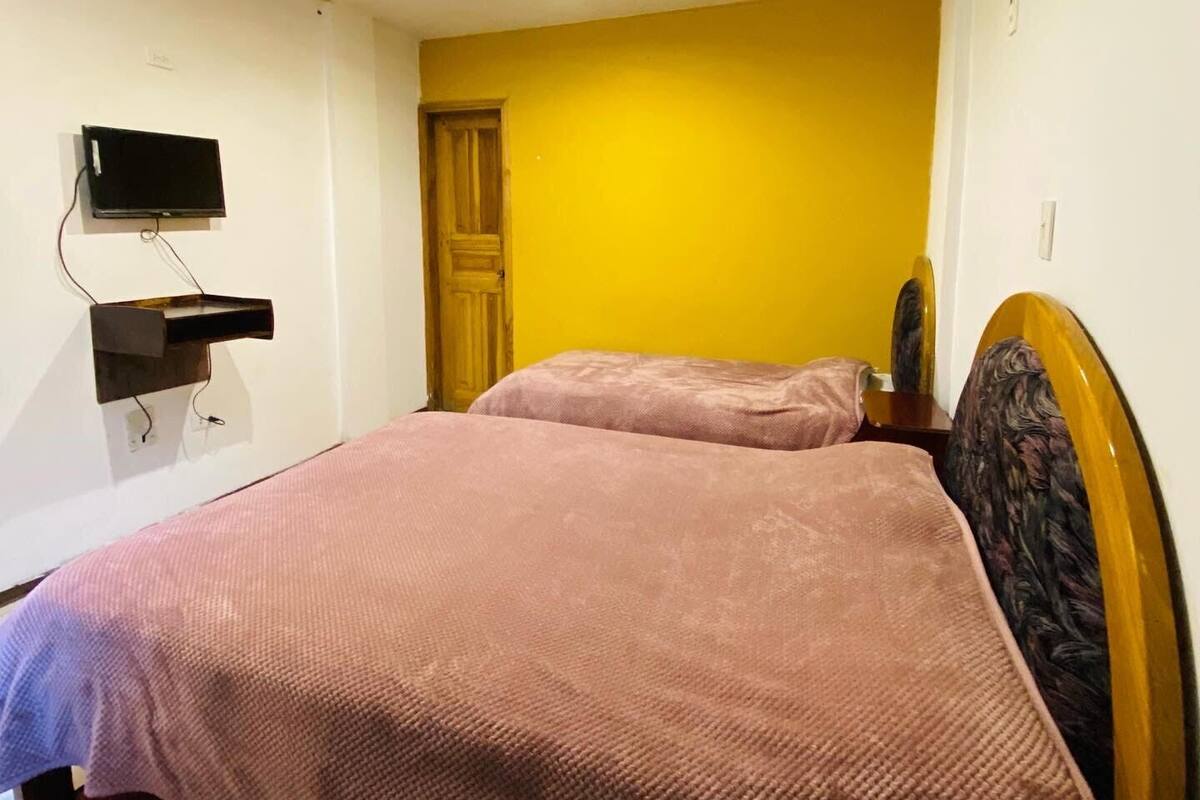 Um quarto com uma cama, televisão na parede e uma porta.