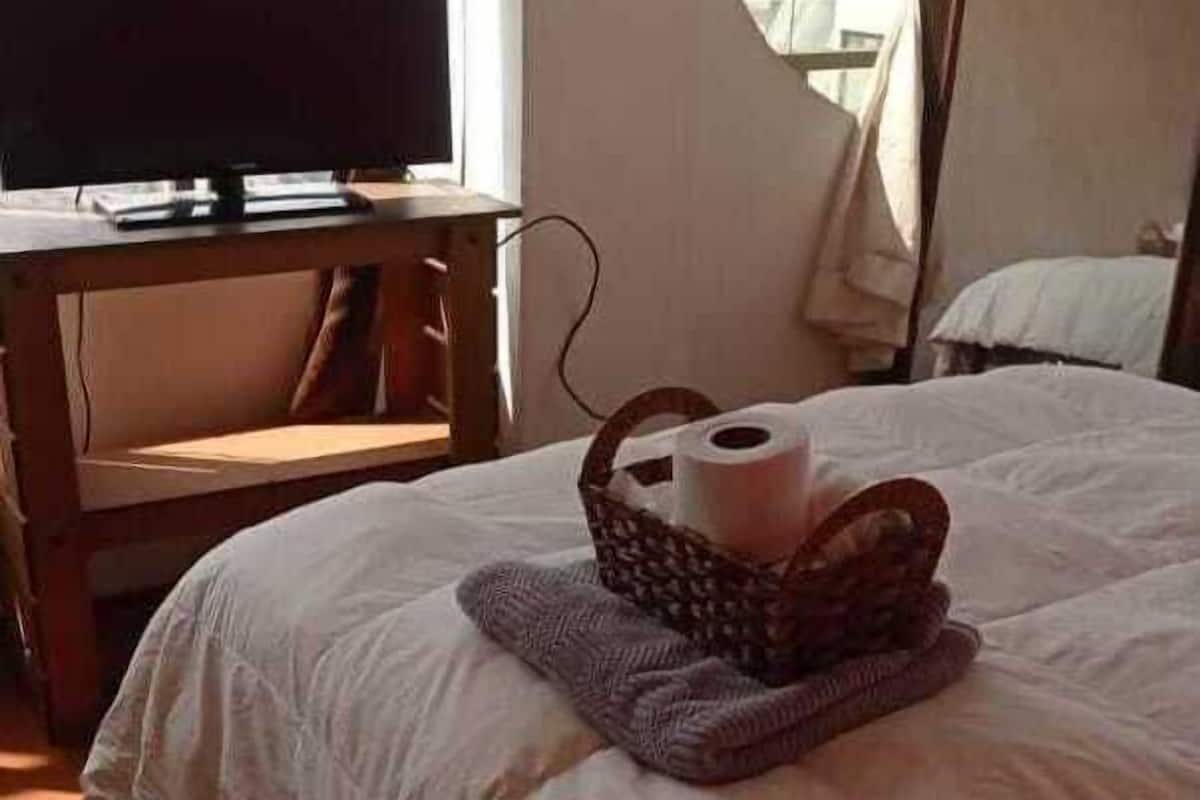 Quarto de hotel com uma cama, uma televisão sobre uma mesa de madeira e uma janela com cortinas.