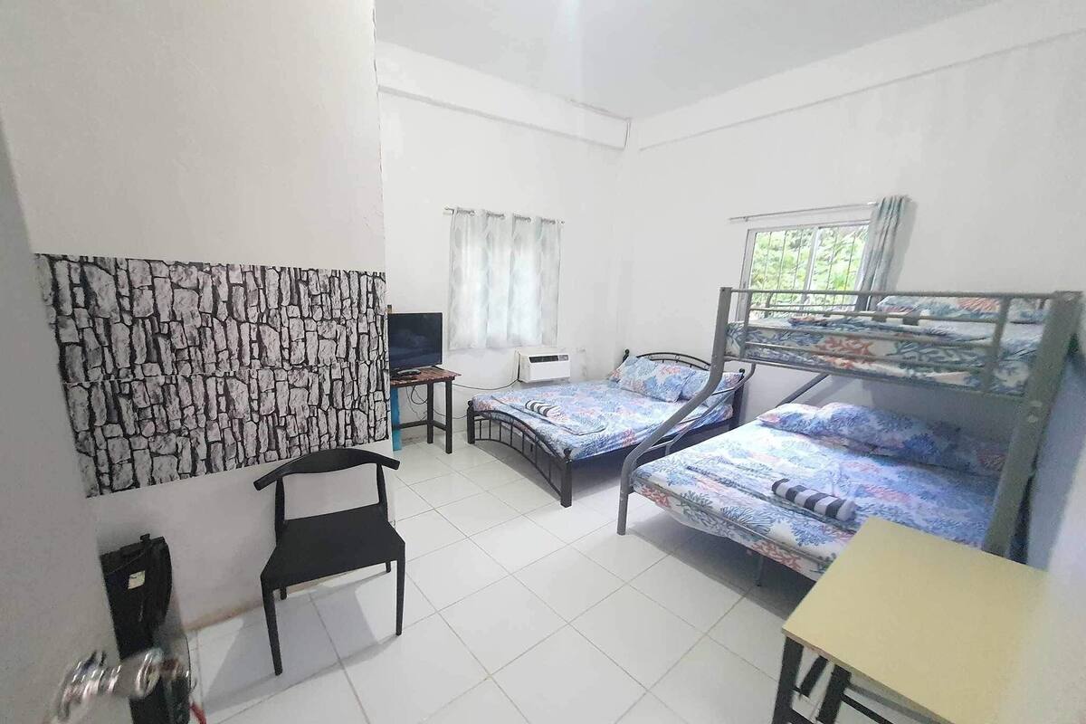 Um quarto de dormitório com beliches, uma escrivaninha, uma cadeira, uma televisão e uma janela com cortinas.
