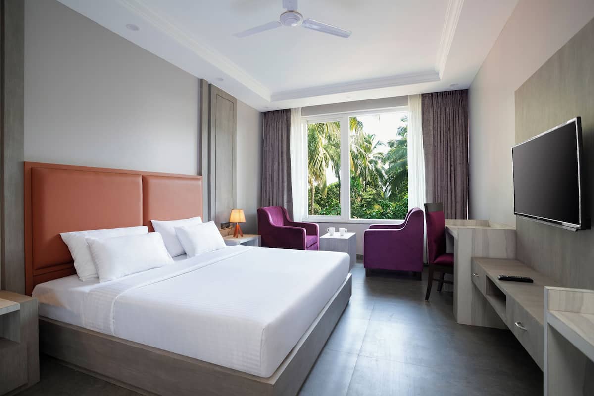Quarto de hotel com cama grande, escrivaninha, cadeira, televisão e janela com cortinas.