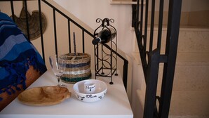 Uma escada com corrimão preto, uma cesta trançada, uma garrafa de vinho, um copo e uma tigela de madeira sobre uma superfície branca.