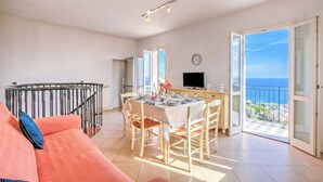 Uma sala de estar espaçosa com uma mesa de jantar, um sofá e uma varanda com vista para o mar.