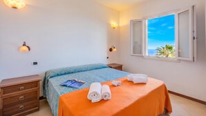 Quarto de hotel com cama, mesa de cabeceira, cômoda e janela com vista para o mar.