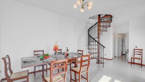 Uma sala de jantar com uma mesa redonda, cadeiras de madeira, um lustre e uma escada em espiral.