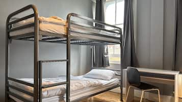 Quarto com beliche, escrivaninha e cadeira, janela com cortinas e vista para o exterior.