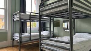 Quarto com beliches, janela com cortinas e vista para um edifício.