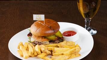 Um prato com hambúrguer, batatas fritas e um copo de cerveja sobre uma mesa de madeira.