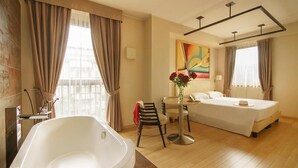 Quarto de hotel com uma banheira grande, uma cama, uma escrivaninha com cadeira e um quadro na parede.