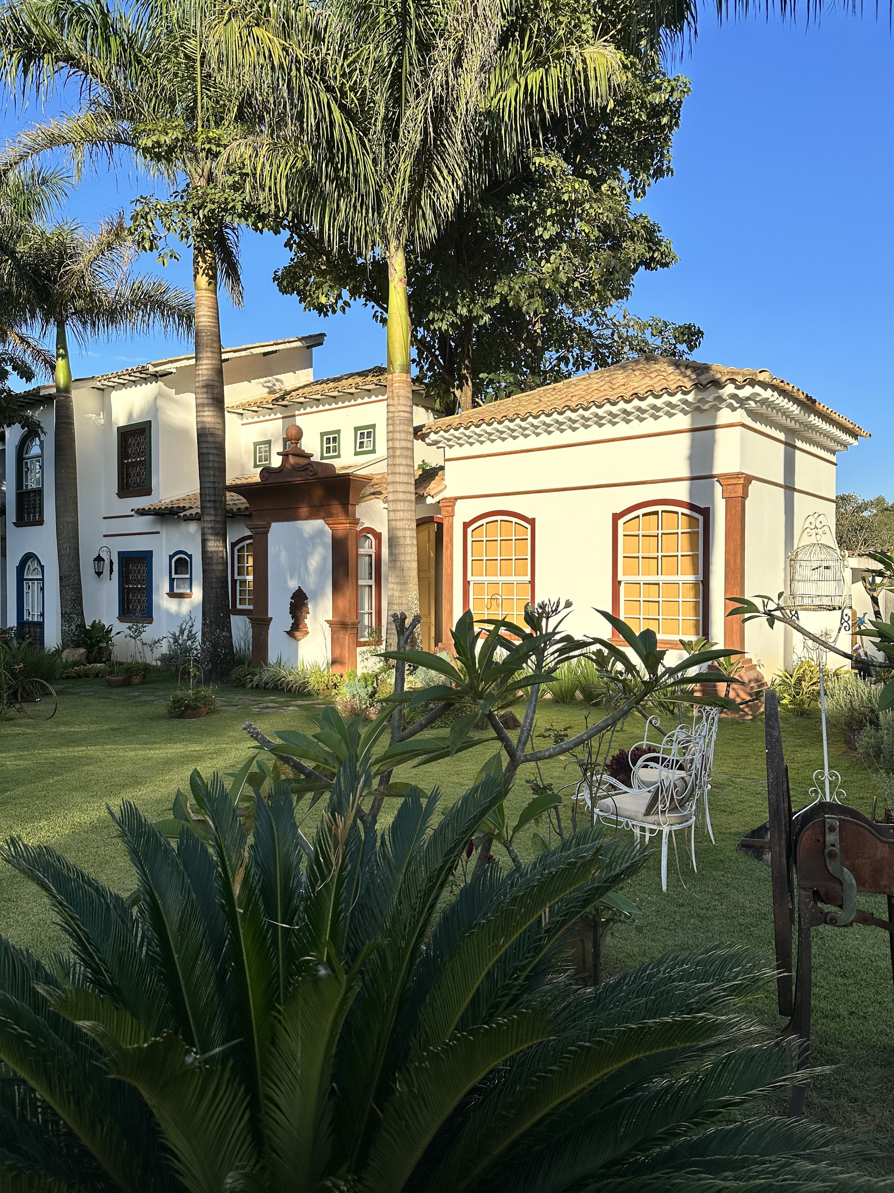 Um edifício colonial tradicional com telhado de cerâmica, janelas grandes e um jardim bem cuidado, com palmeiras e gramado.