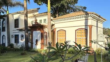 Um edifício colonial tradicional com telhado de cerâmica, janelas grandes e um jardim bem cuidado, com palmeiras e gramado.