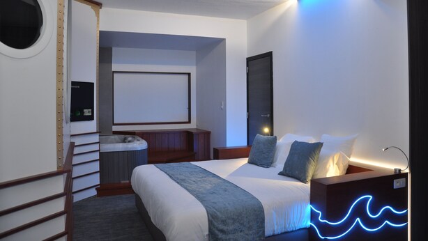 Quarto de hotel moderno com cama, mesa de cabeceira e escrivaninha embutida com cadeira.
