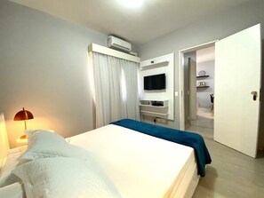 Quarto de hotel com cama, televisão na parede e porta para outro quarto.