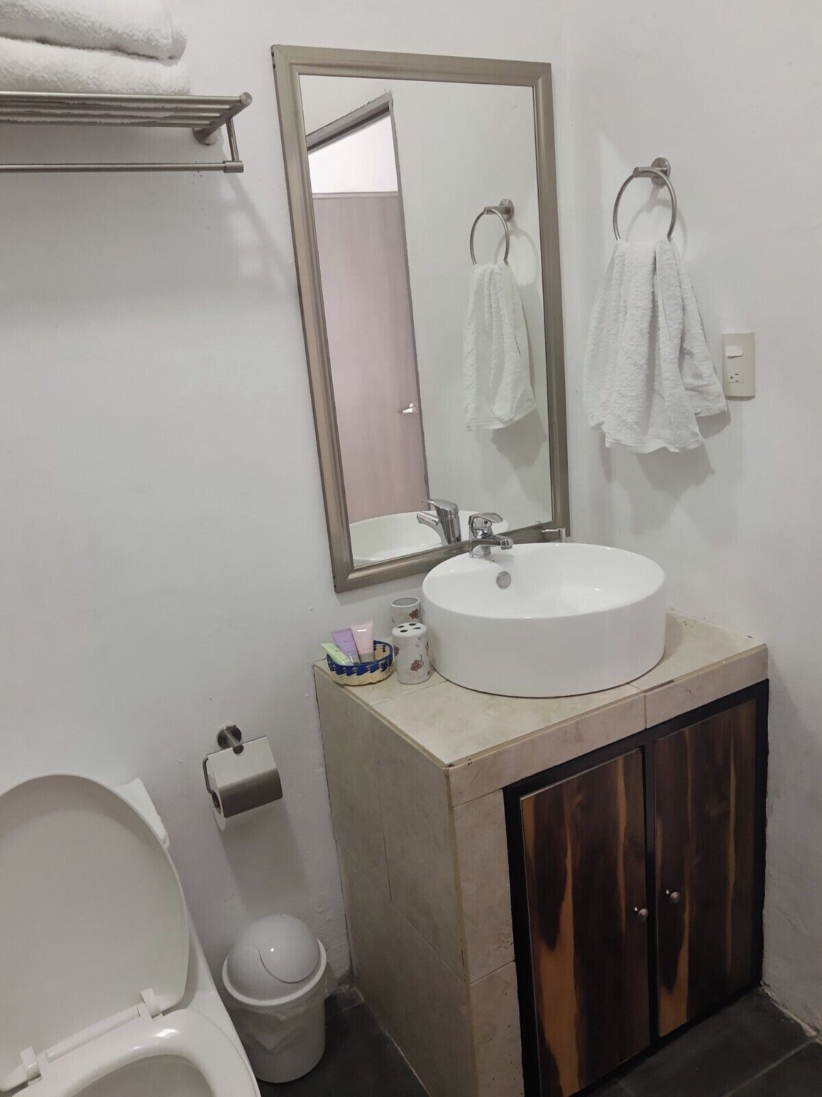 Casa de banho com uma pia branca, um espelho, um porta-toalhas e uma sanita.
