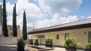 Um edifício com telhado plano, plantas em vasos e um pátio pavimentado.