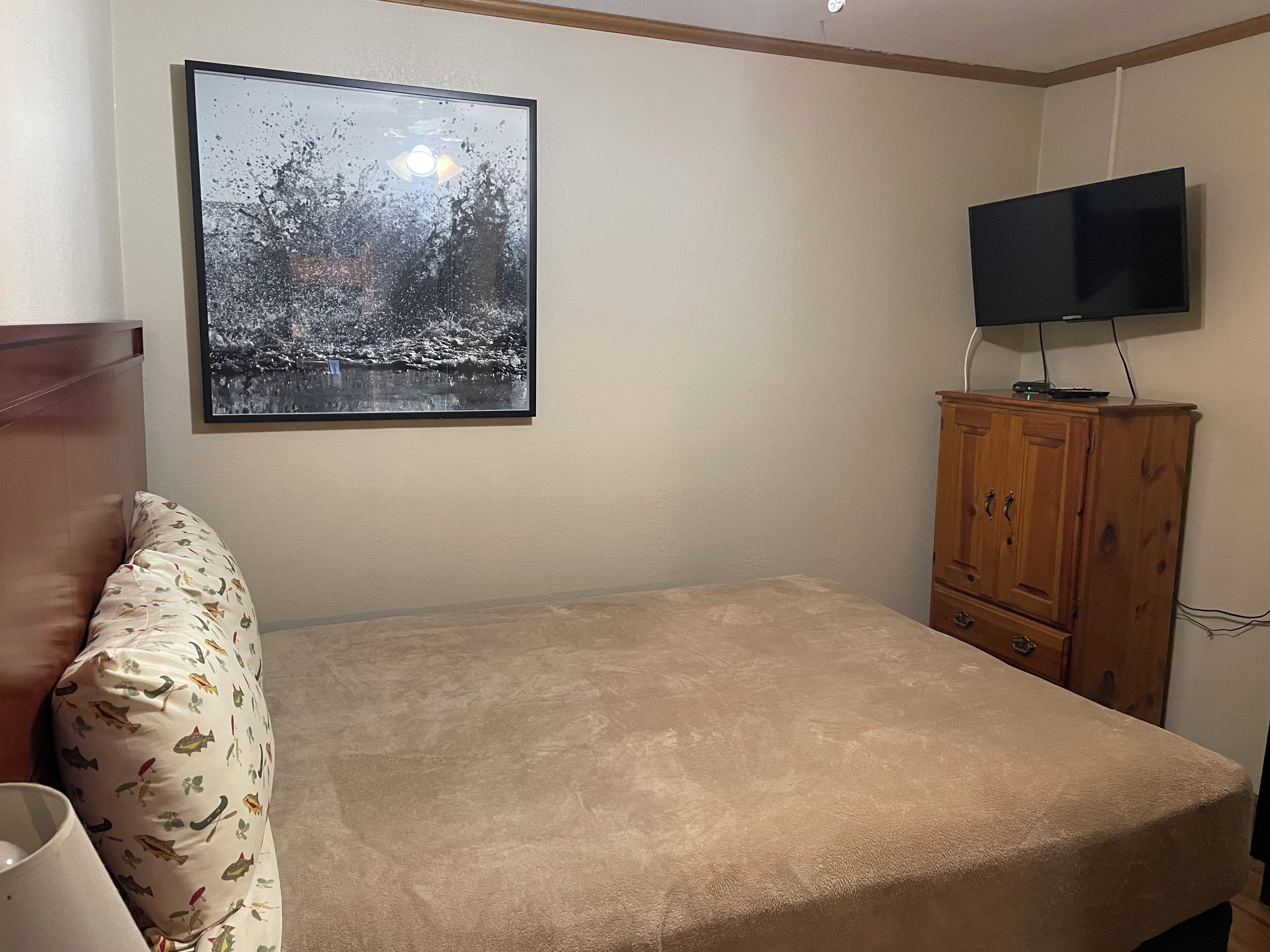 Um quarto com uma cama, um guarda-roupa de madeira, uma TV e um quadro na parede.