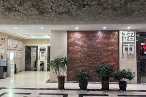 Um hall de hotel com uma parede decorativa, plantas em vasos e uma área de recepção.