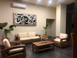 Uma sala de estar com um sofá, duas cadeiras de vime, uma mesa de centro e um objeto decorativo na parede.