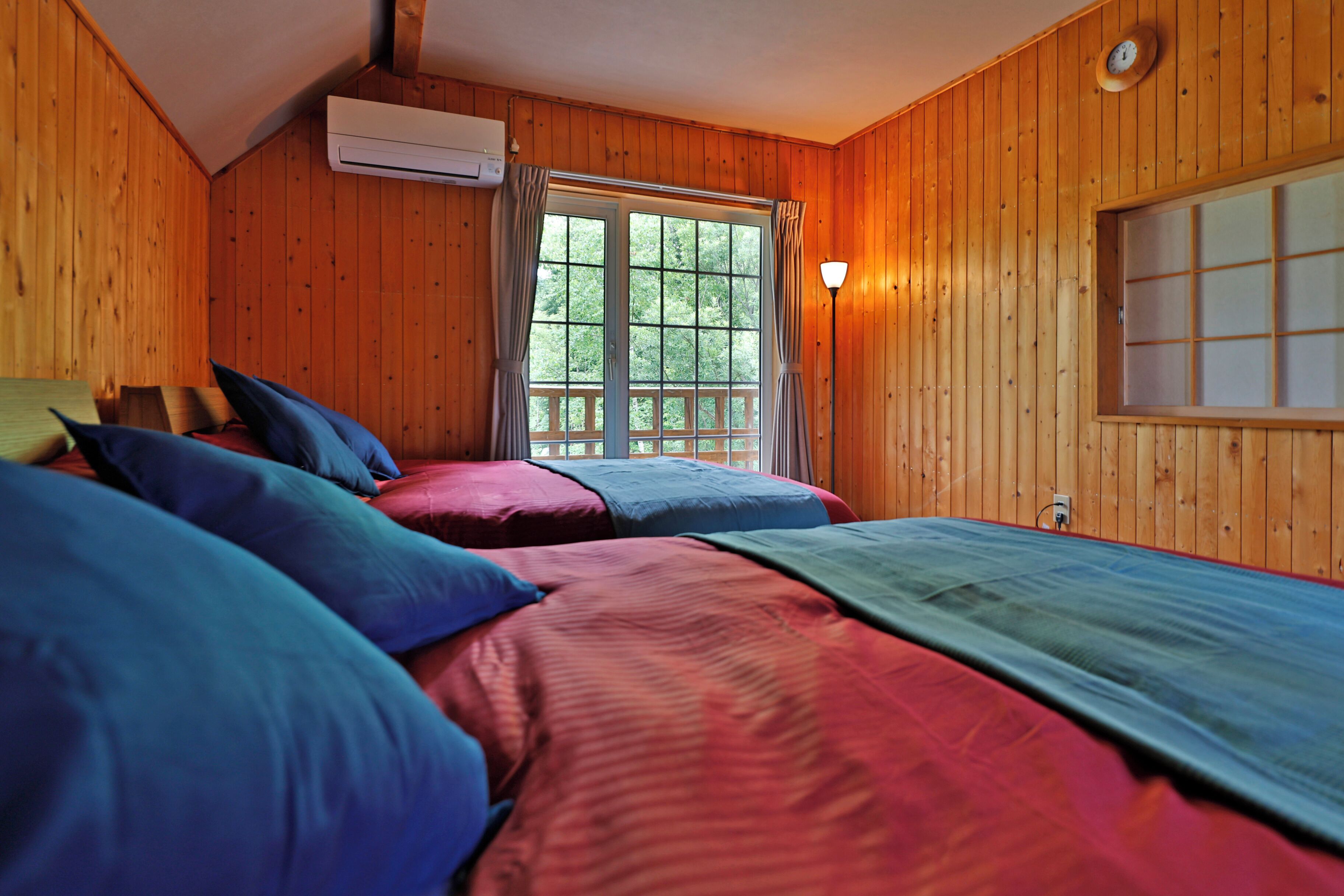 Quarto de cabana de madeira com duas camas, uma janela com cortinas e um aparelho de ar condicionado.