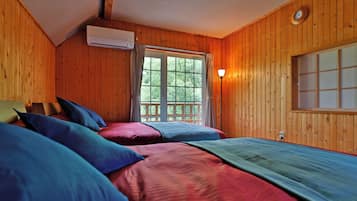 Quarto de cabana de madeira com duas camas, uma janela com cortinas e um aparelho de ar condicionado.